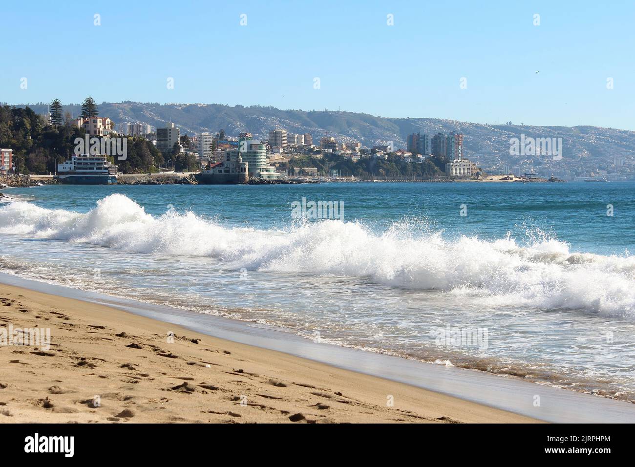Waves on a beach, with a view of the city of Valparaiso, Chile, in the ...