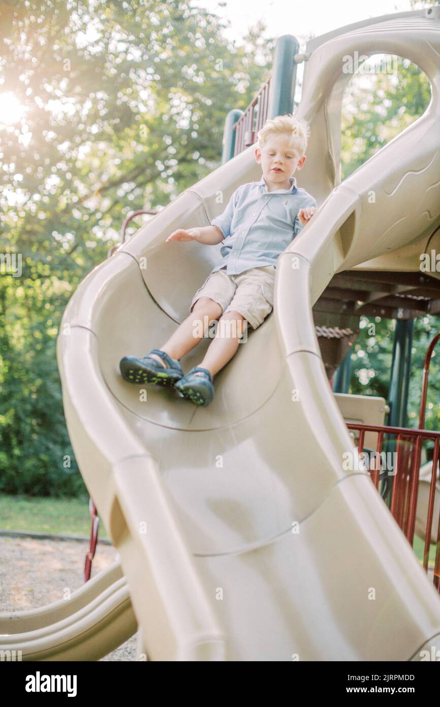 Blonde 5 year-old boy slides down a playground slide at sunset Stock ...