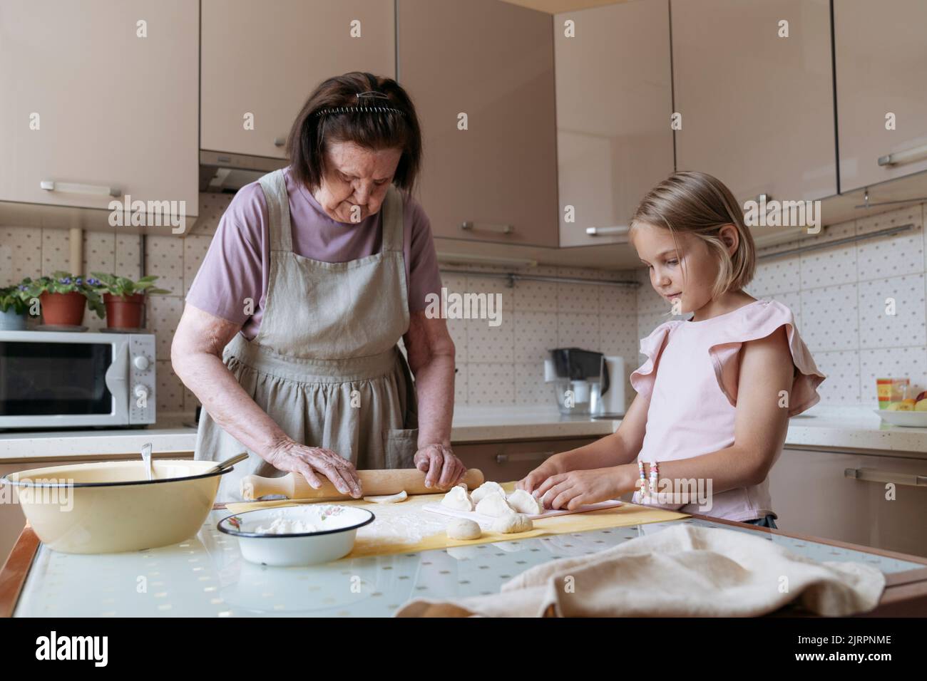 The granddaughter helps the grandmother to make pies in the kitchen ...