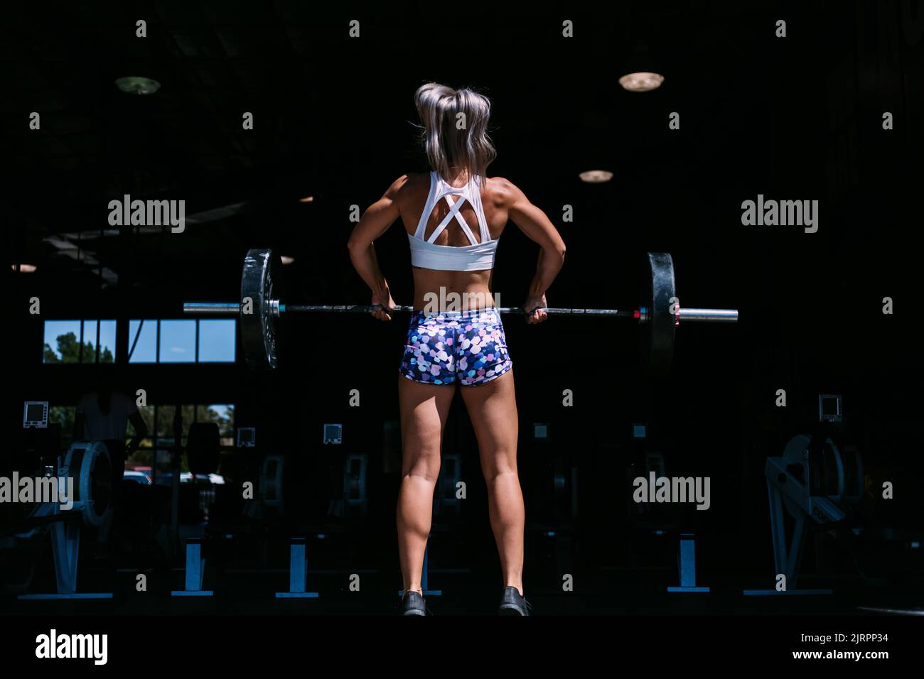 Fit female doing a clean with barbell with a dark gym in the bac Stock ...