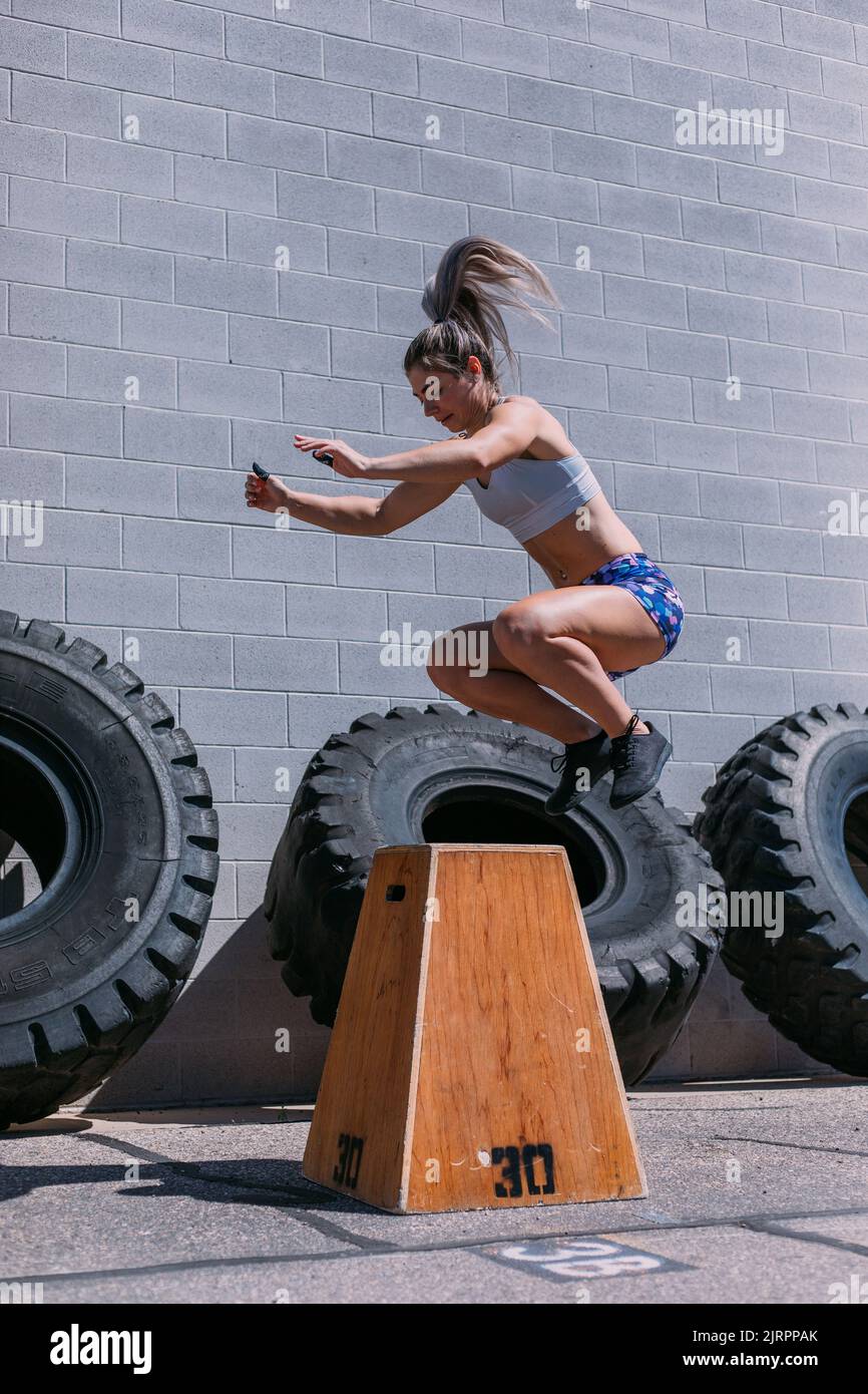 Woman doing a box jump outside onto a brown 30 inch box with tir Stock ...