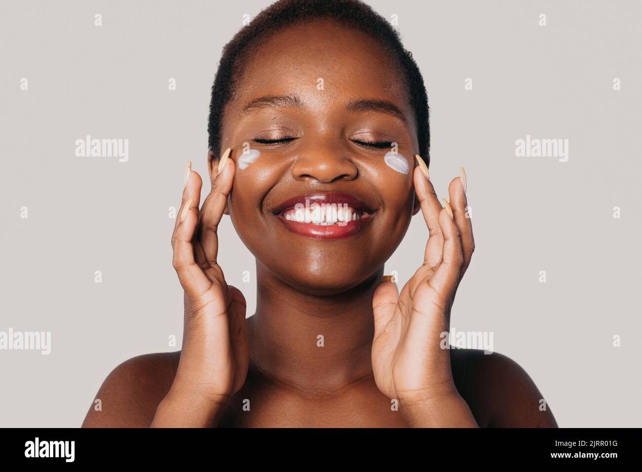 Front view portrait of an afro woman applying face cream onto her ...