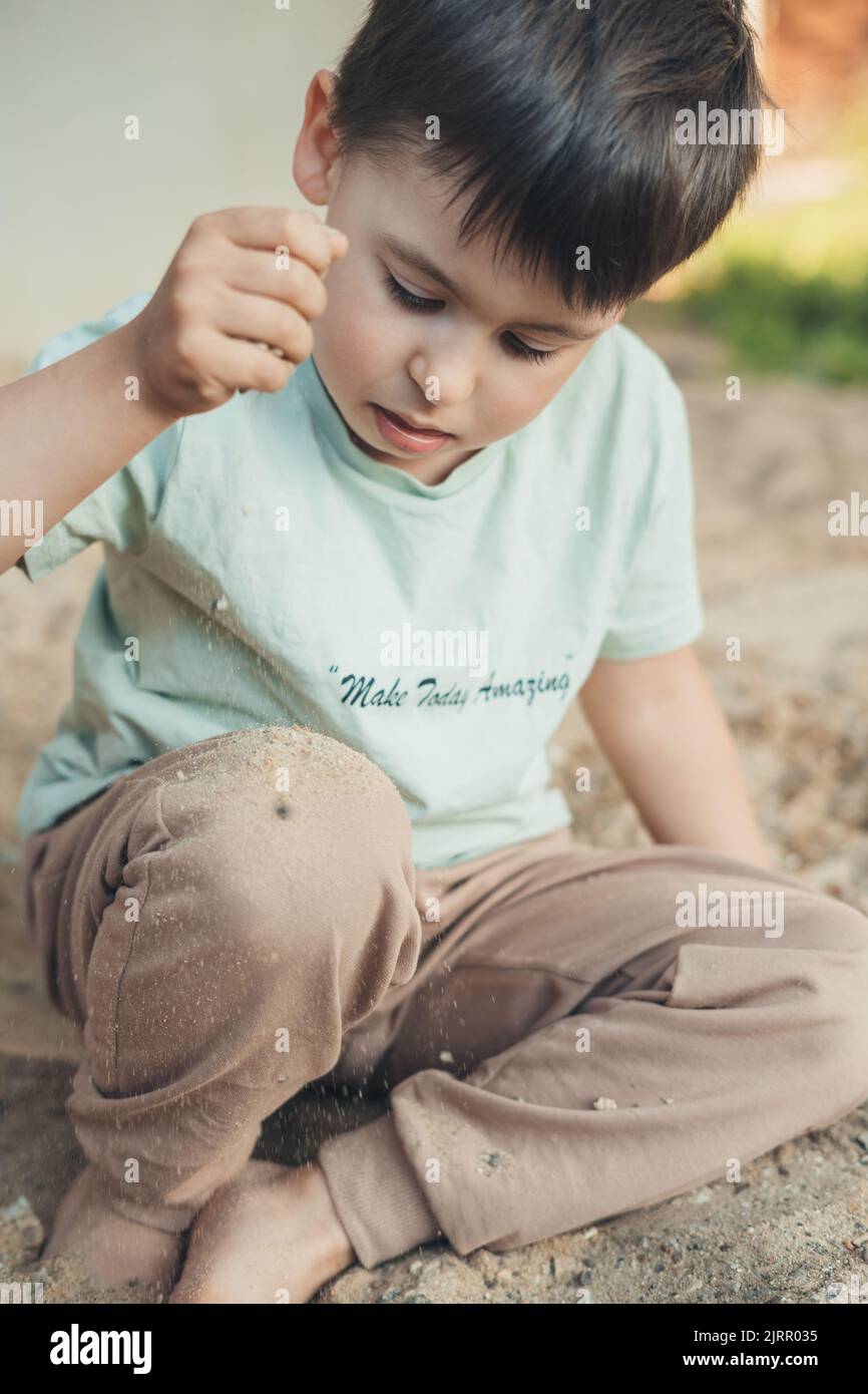 Little boy looking intently and concentrated at the sand flowing from ...