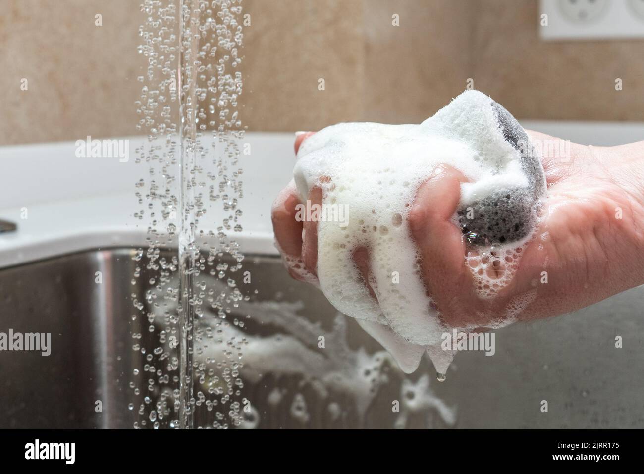 Female hand squeezes a sponge with foam on the background of the ...