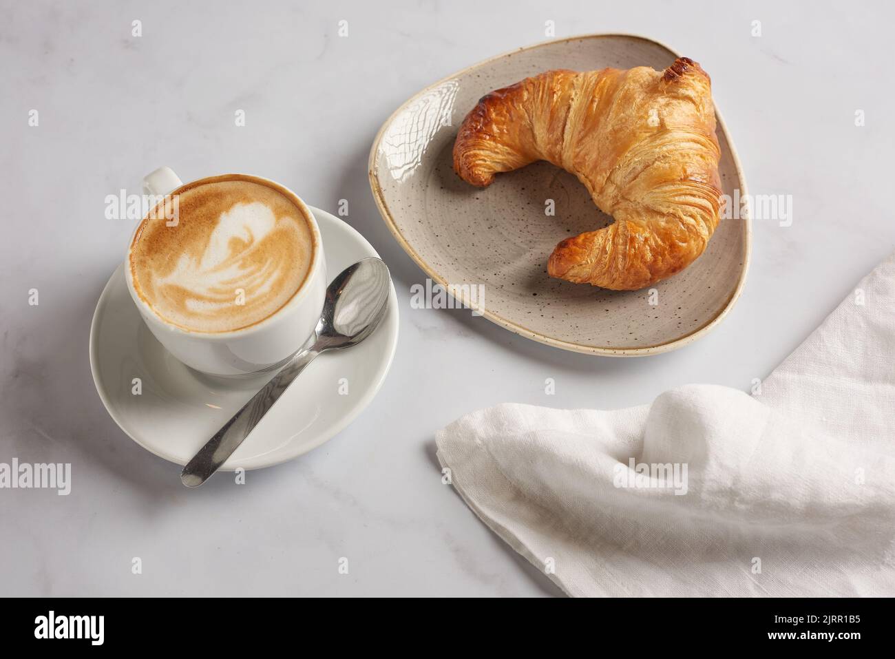 A French croissant with coffee and small spoon on marble surface Stock ...