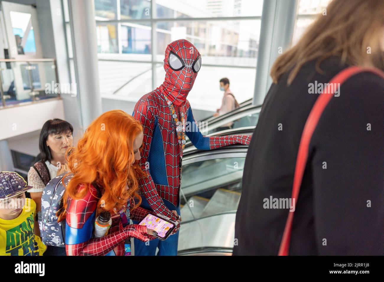 People dressed as comic book characters ride an escalator at Fan Expo ...