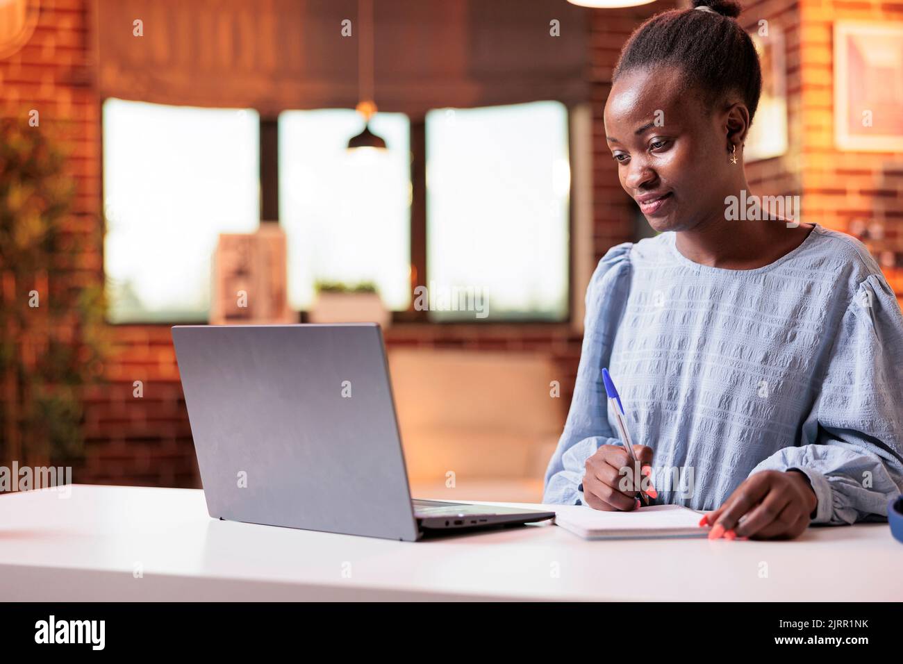 Woman studying with laptop and taking notes in notebook. Female african ...
