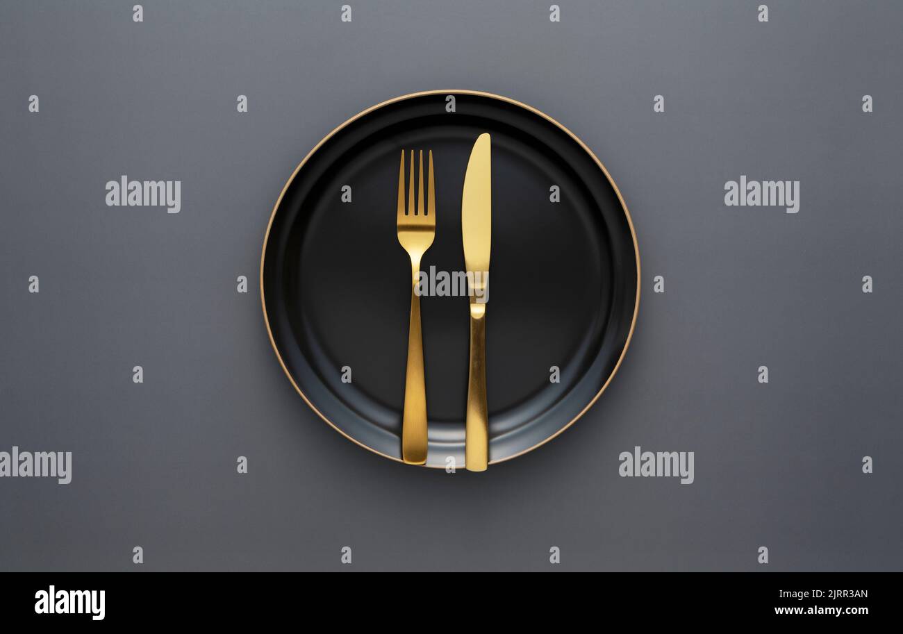 Gold knives and forks on a black background, empty black plate ...