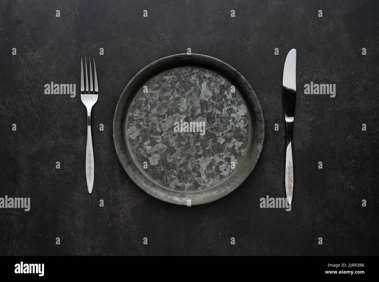 Silver knives and forks on a black background, empty iron plates ...