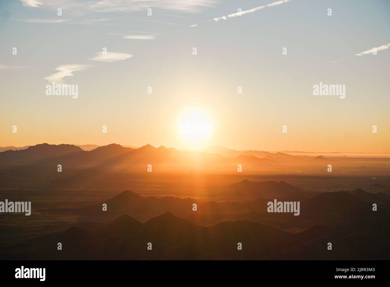 The flaming orange sun rises over a range of mountains in early morning, making them look like ...