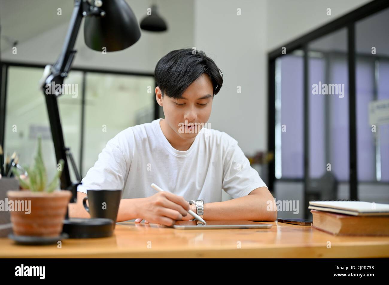 Good looking young Asian man at his working desk, using digital tablet ...