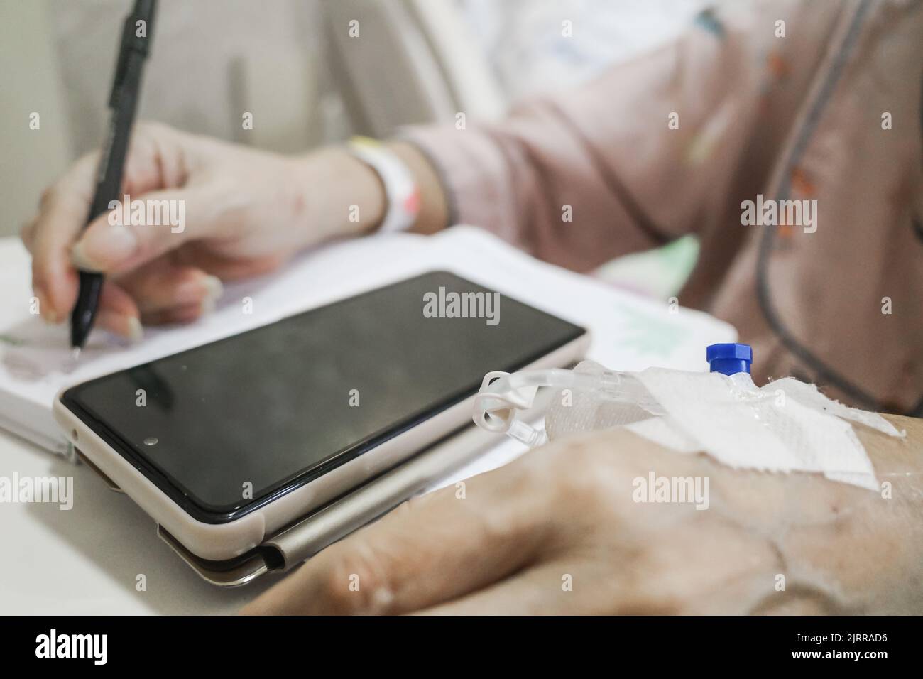 Female patient sitting on bed in hospital room and writing on book with ...