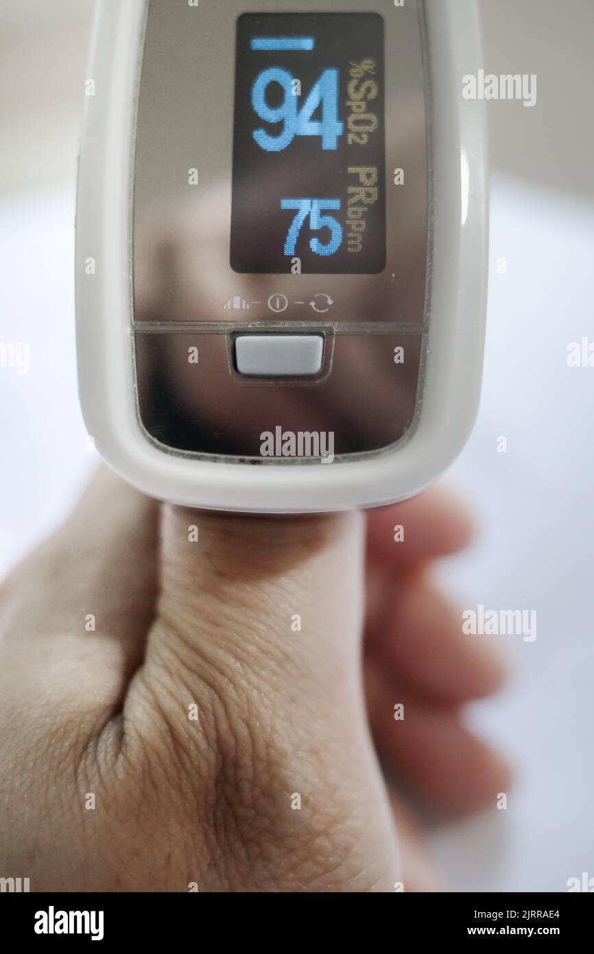 Patient on hospital bed using oximeter on thumb for measuring pulse and ...