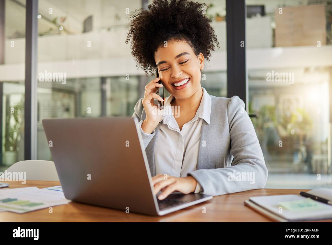 Business woman working on laptop in office, in conversation on phone ...