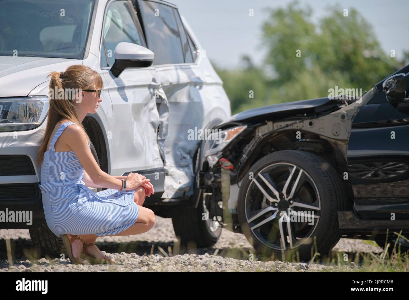 Sad young woman driver sitting near her smashed car looking shocked on ...