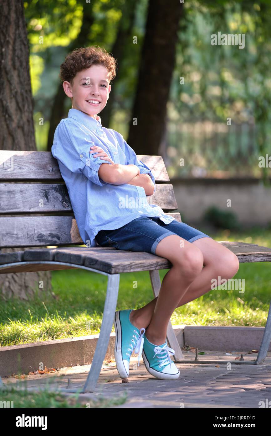 Young happy child boy relaxing sitting on bench in summer park ...