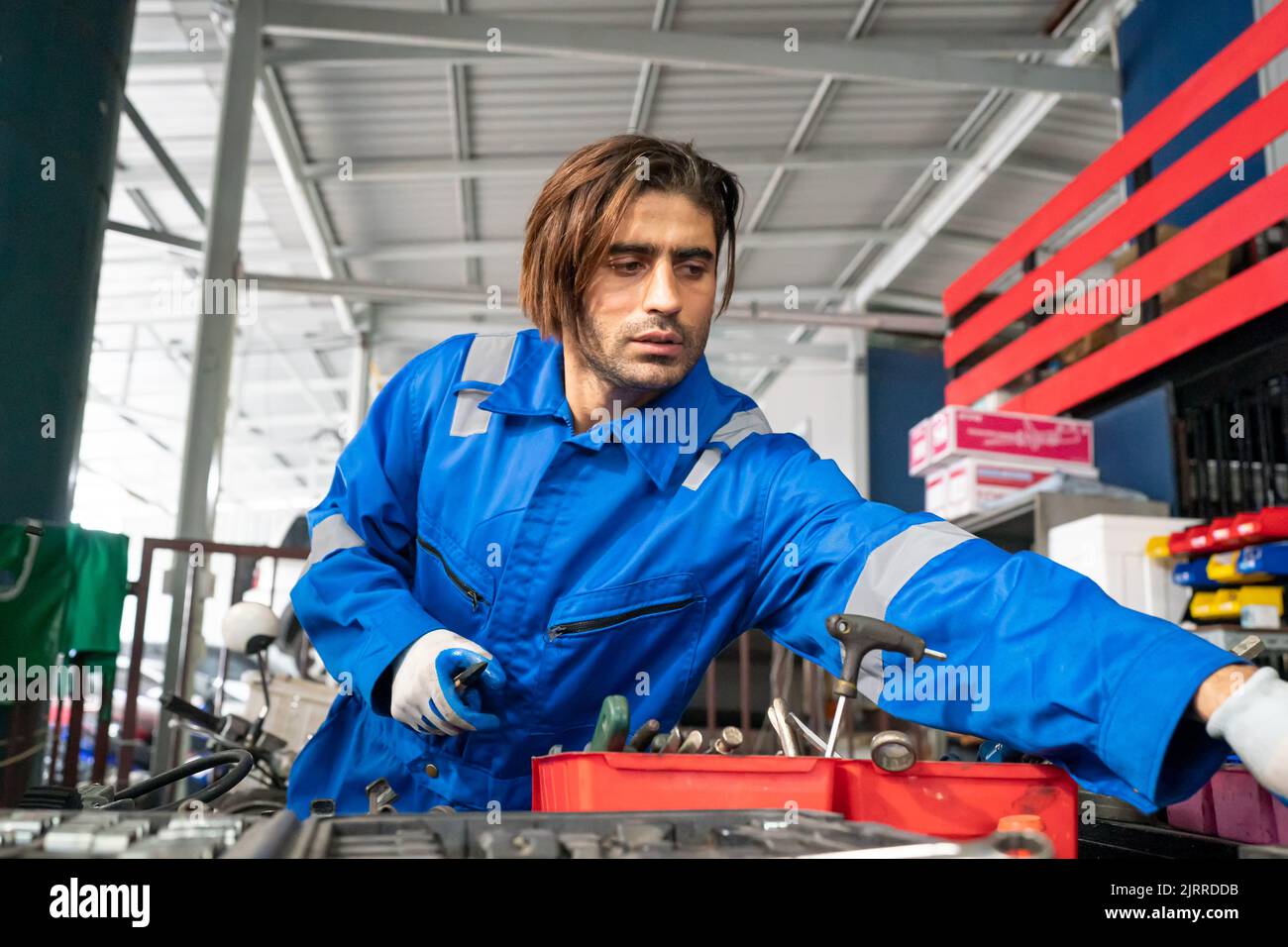 Male car operator wearing blue overalls, gloves working under the hood ...