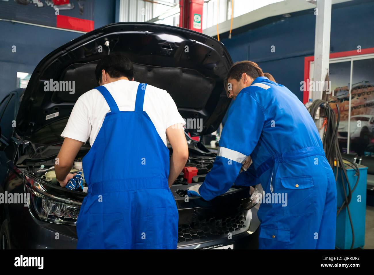 Male car operator wearing blue overalls, gloves working under the hood ...
