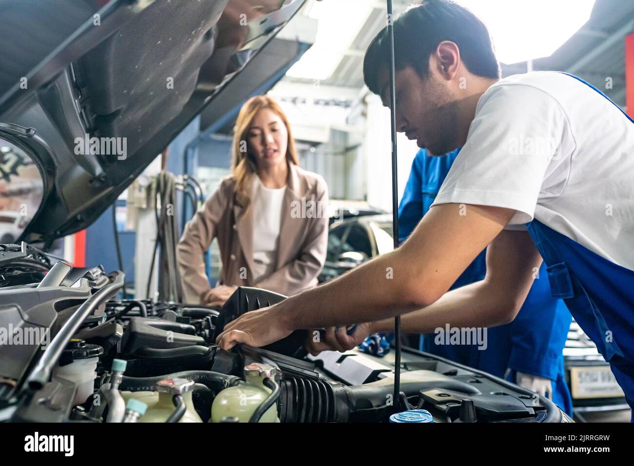 Male car operator wearing blue overalls, gloves working under the hood ...