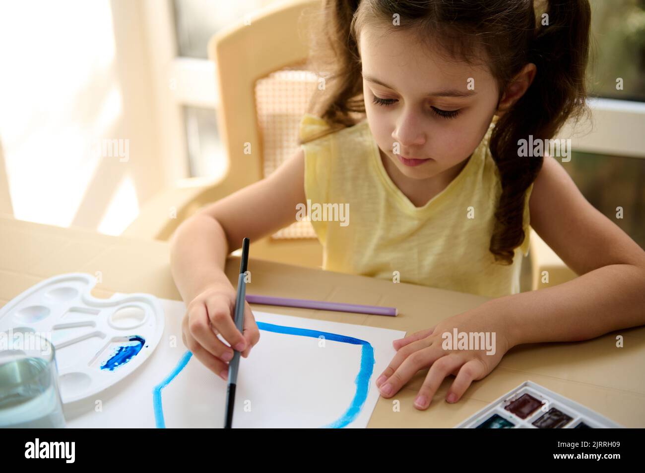 Close-up of a primary school student painting with watercolor paints ...