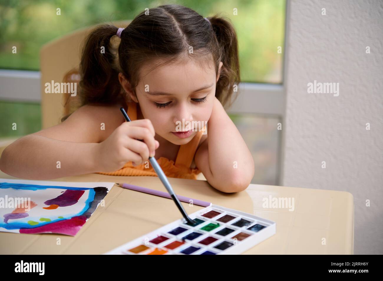 Concentrated Caucasian preschooler girl mixing watercolors paints with ...