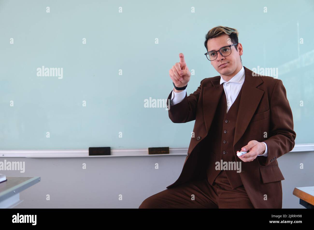 A teacher in a suit pointing towards the class. Teacher in front of the ...