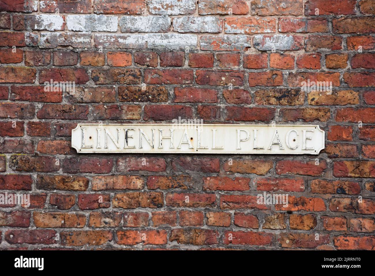 A faded street name sign for Linenhall Place mounted on a red brick ...