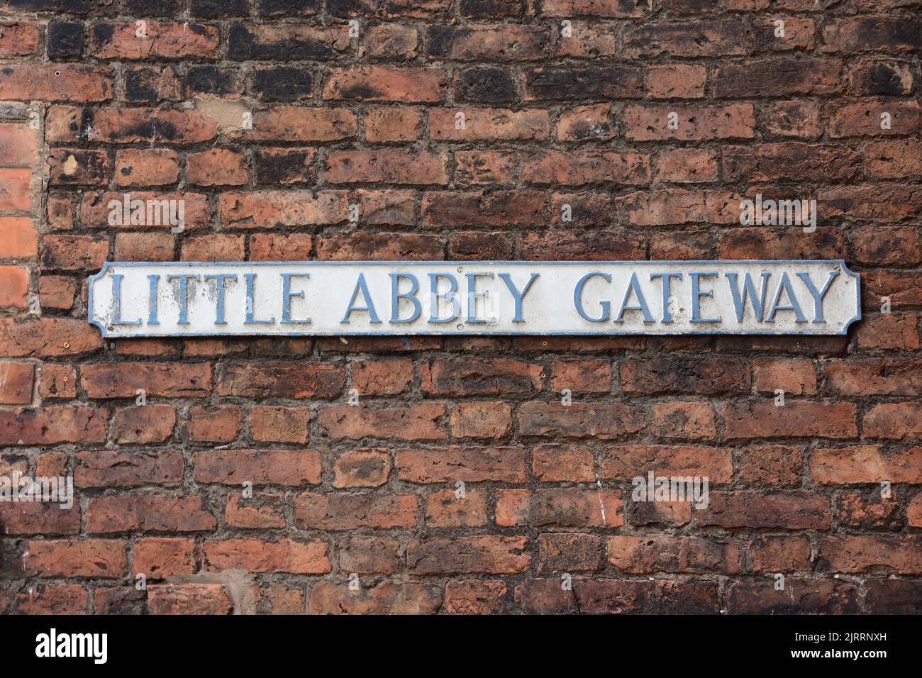 A faded street name sign for Little Abbey Gateway mounted on a red ...