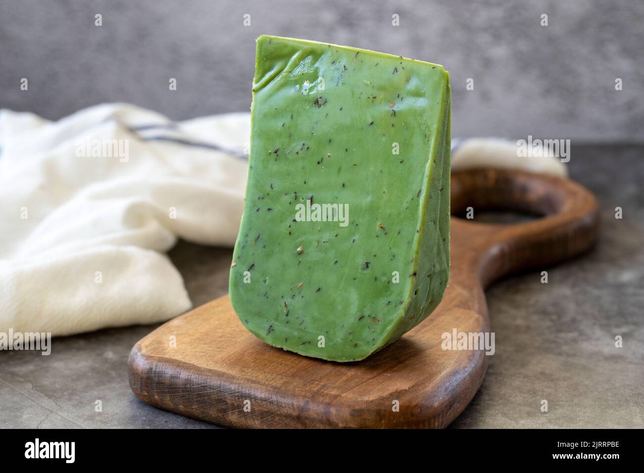 Green gouda cheese. Gouda cheese with basil on a dark background. Dutch ...