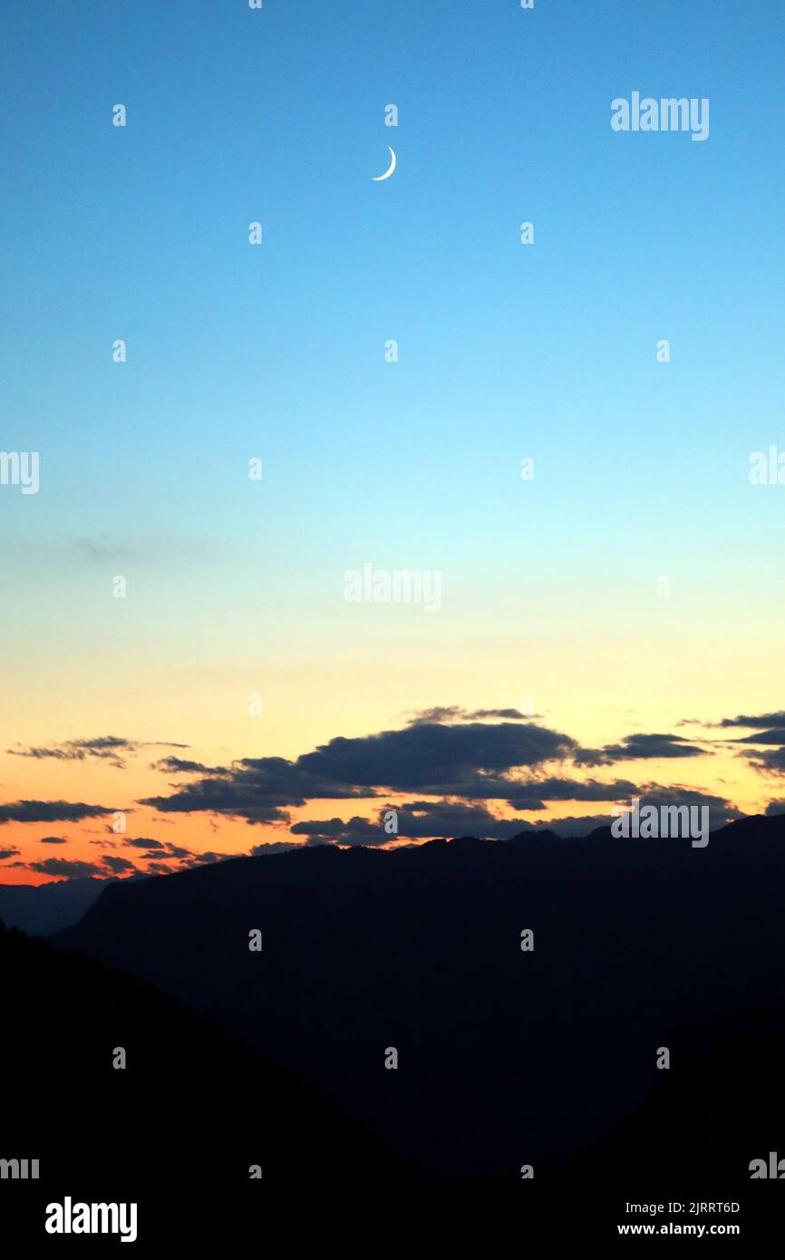 narrow band of the moon with the colorful setting sun and black outline ...
