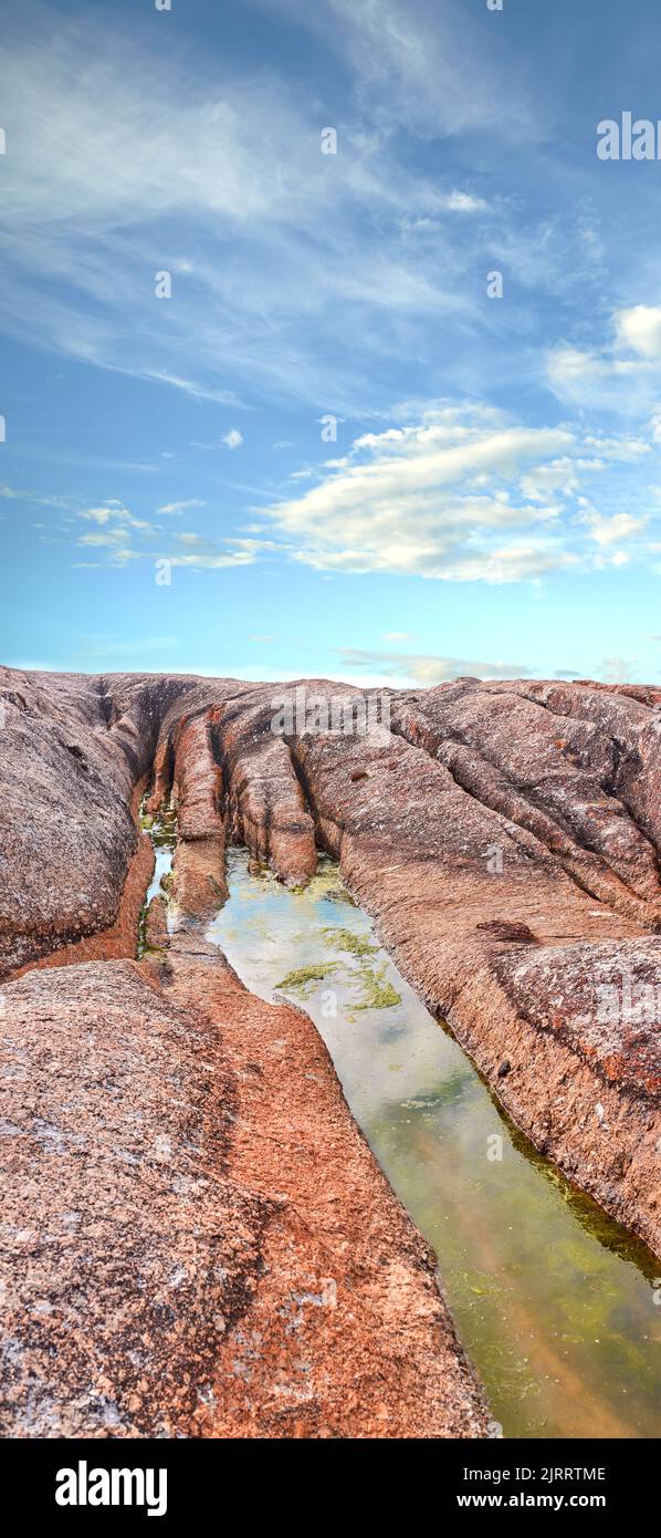 Stream, water or inlet on rocky terrain outside under cloudy blue sky ...