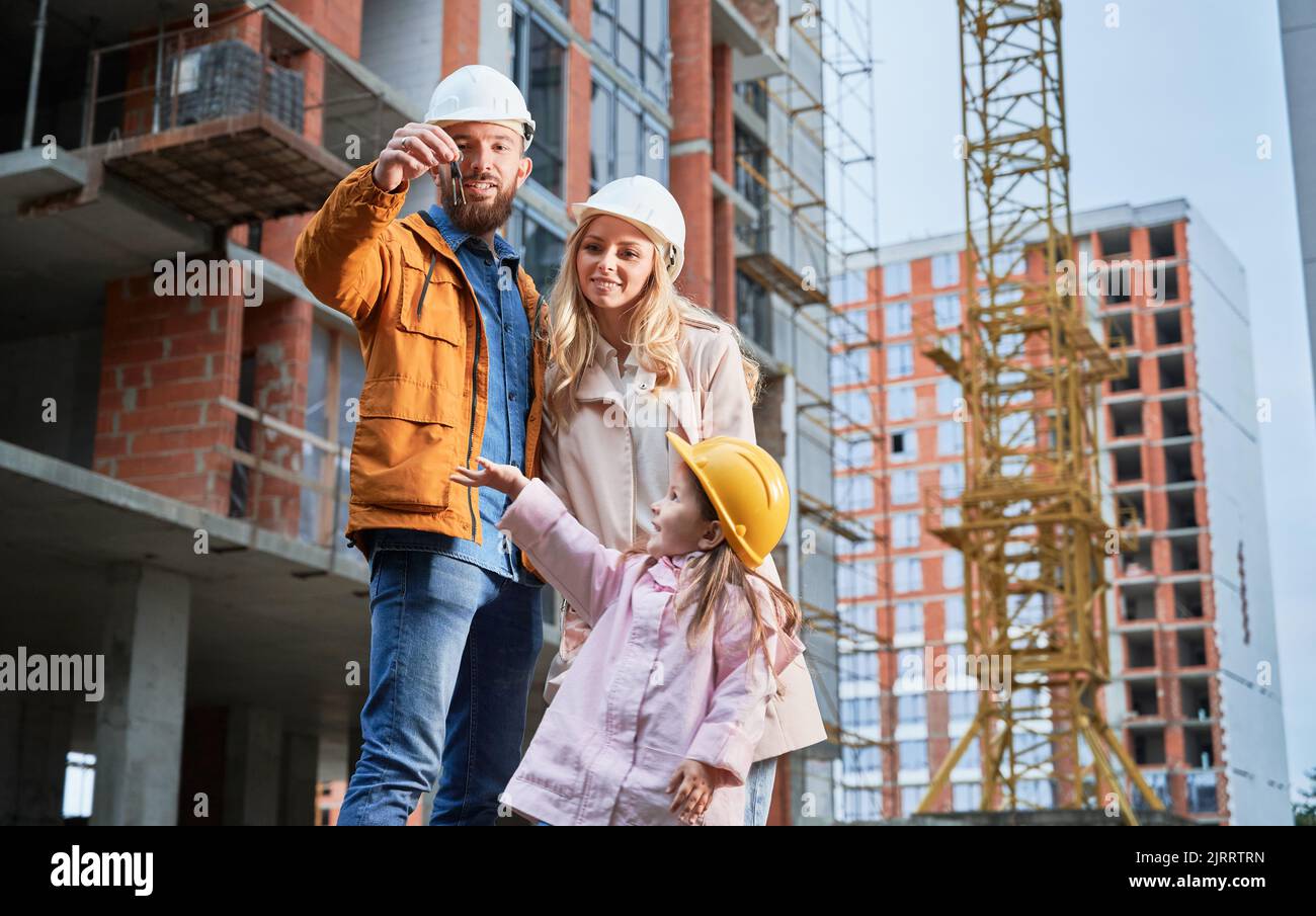 Man holding apartment keys and smiling while standing next to wife and daughter outside building ...