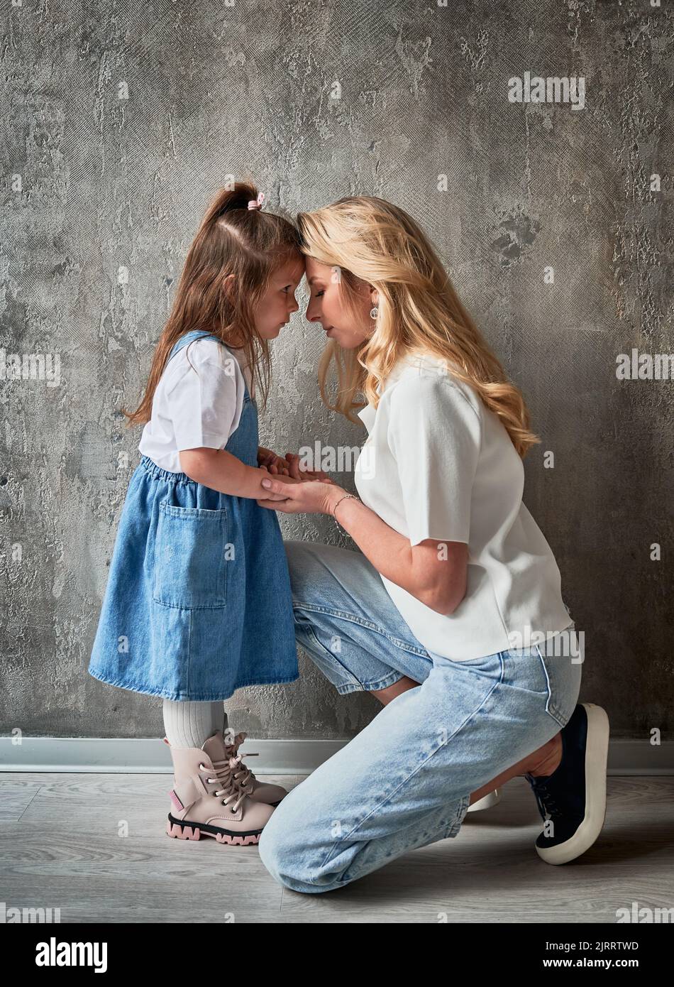 Side view of cute child with mother standing against the wall at home ...