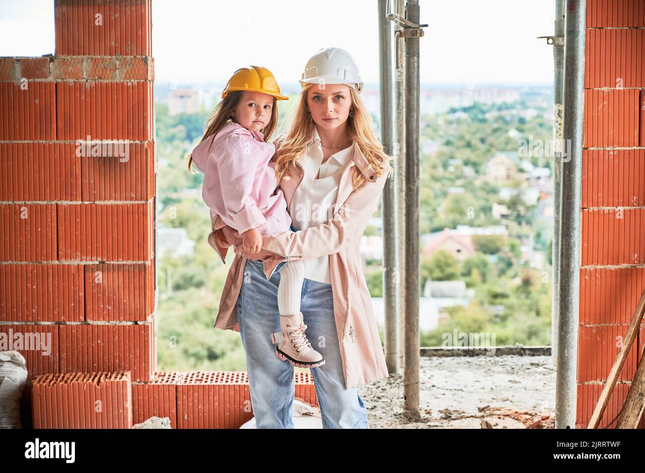 Front view of woman in building helmet holding child and looking at ...