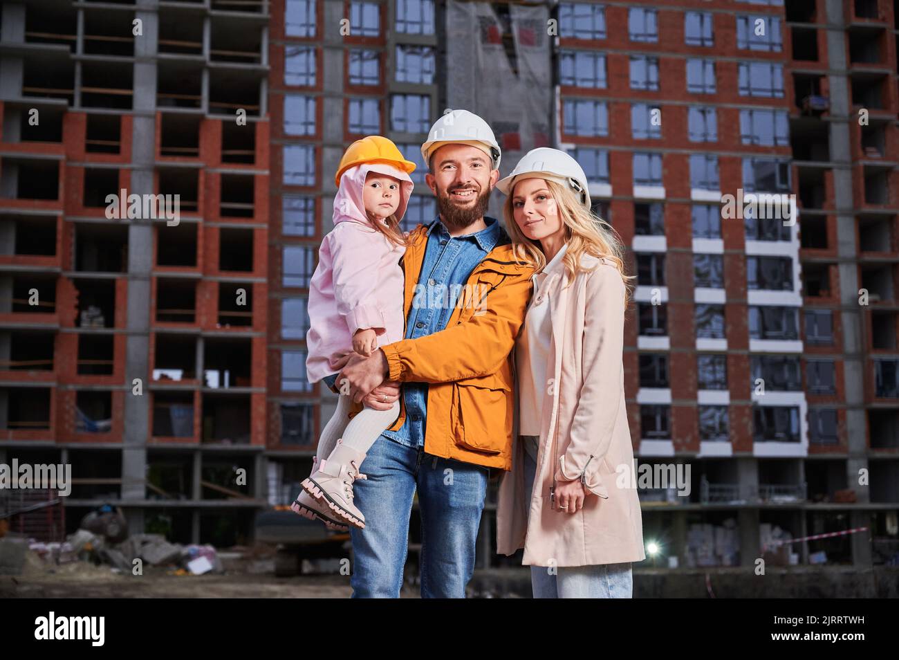 Parents and daughter smiling while standing outdoors against apartment ...