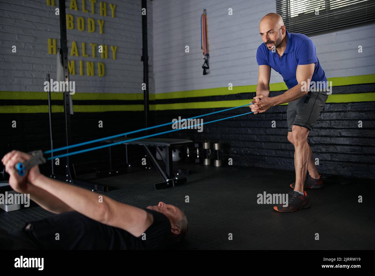 Male personal trainer holds onto elastic rubber resistance bands while ...
