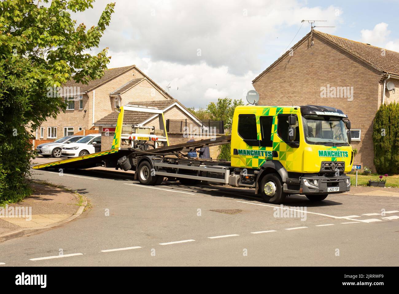 A green and yellow large transporter lowering ramp to collect cars at a ...