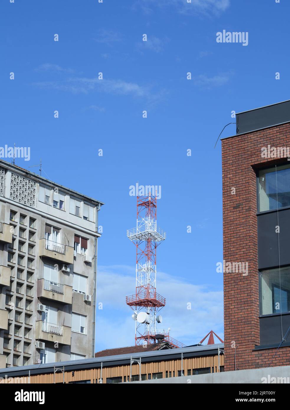 metal transmission tower in a town with a blue sky behind it and buildings on a left and right ...