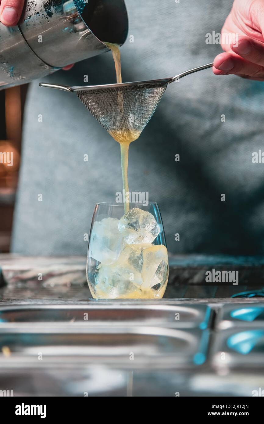 At a luxury nightclub, the bartender strains his cocktail into a glass ...