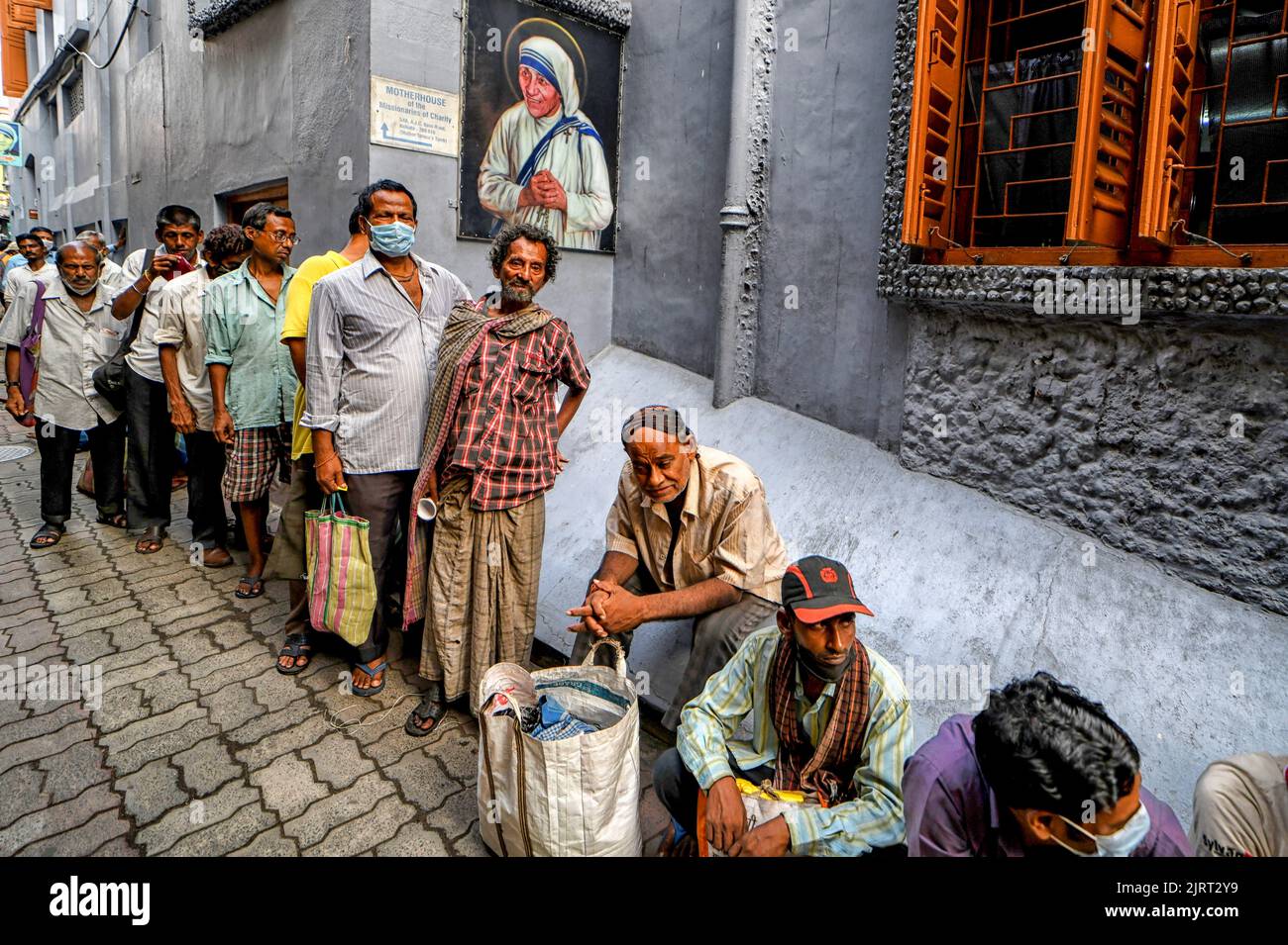 Underprivileged people stand in queues under a picture of Mother Teresa ...