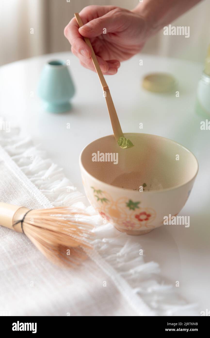 A vertical shot of hand pouring matcha powder in a bowl with a spoon ...