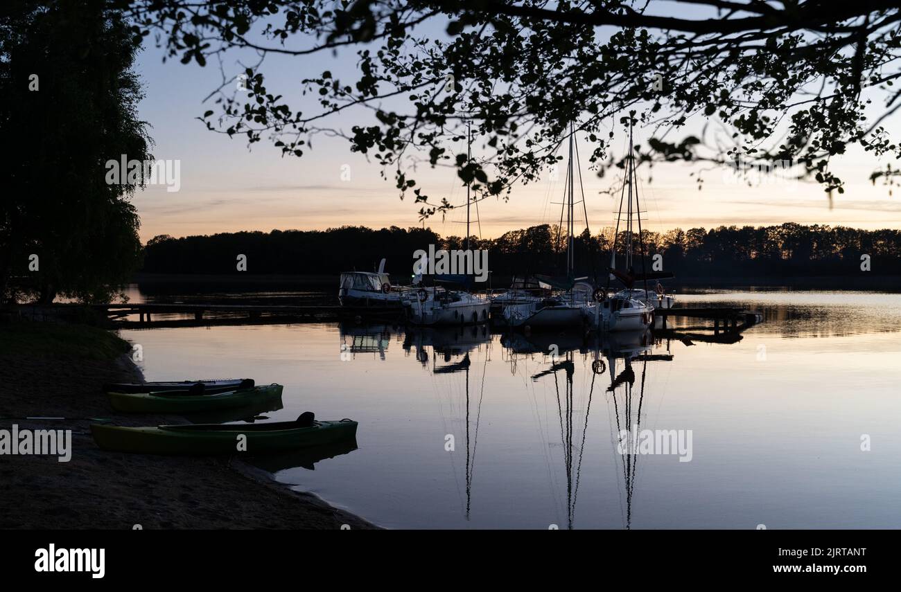 The sky and boats reflected on the water with trees in the background ...