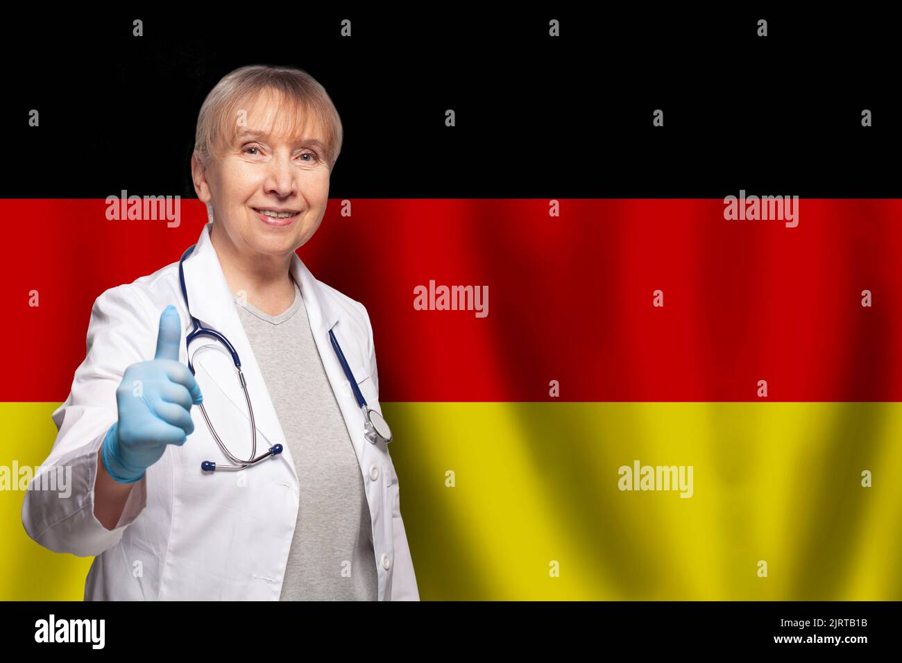 German smiling mature doctor woman holding stethoscope on flag of ...