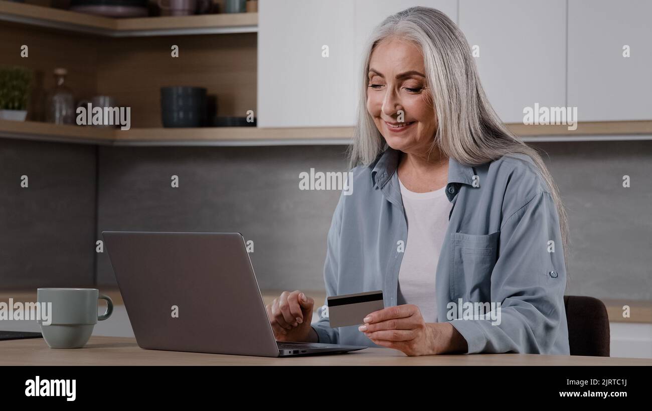 Happy old female caucasian consumer grey-haired granny shopper pay ...