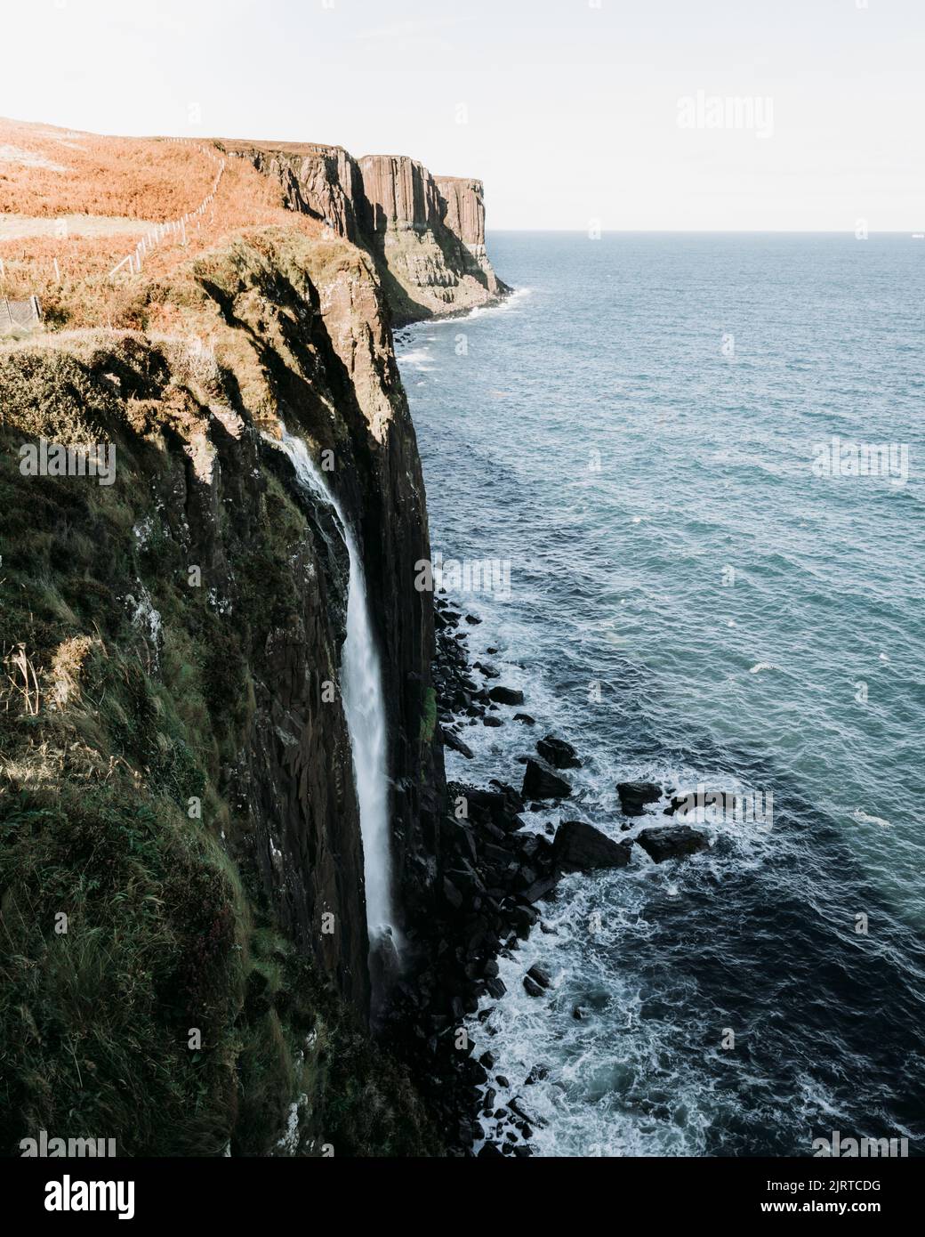 A vertical shot of a waterfall flowing on a rocky cliff on the Isle of ...