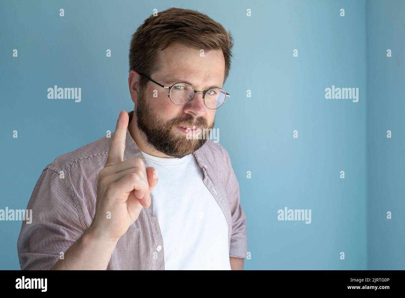 Strict bearded man in glasses raises index finger up, as if reminding ...