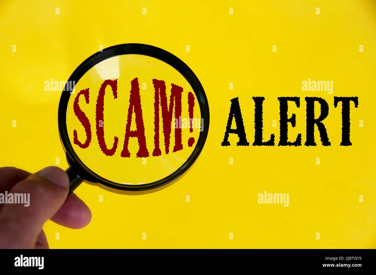 Scam alert text on yellow cover with hand holding magnifying glass ...