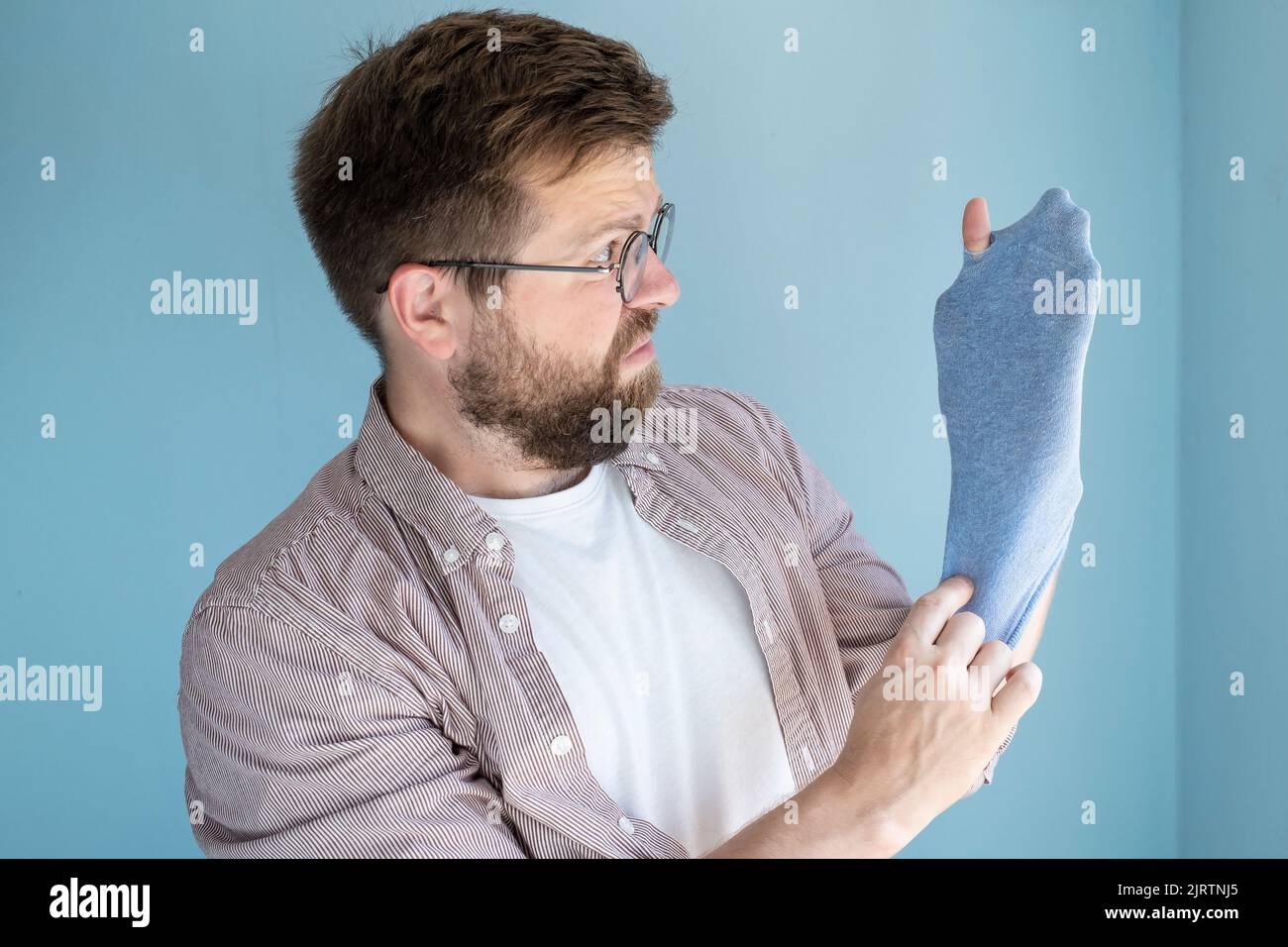 Frowning man put his holey worn sock on hand from which fingers stick ...