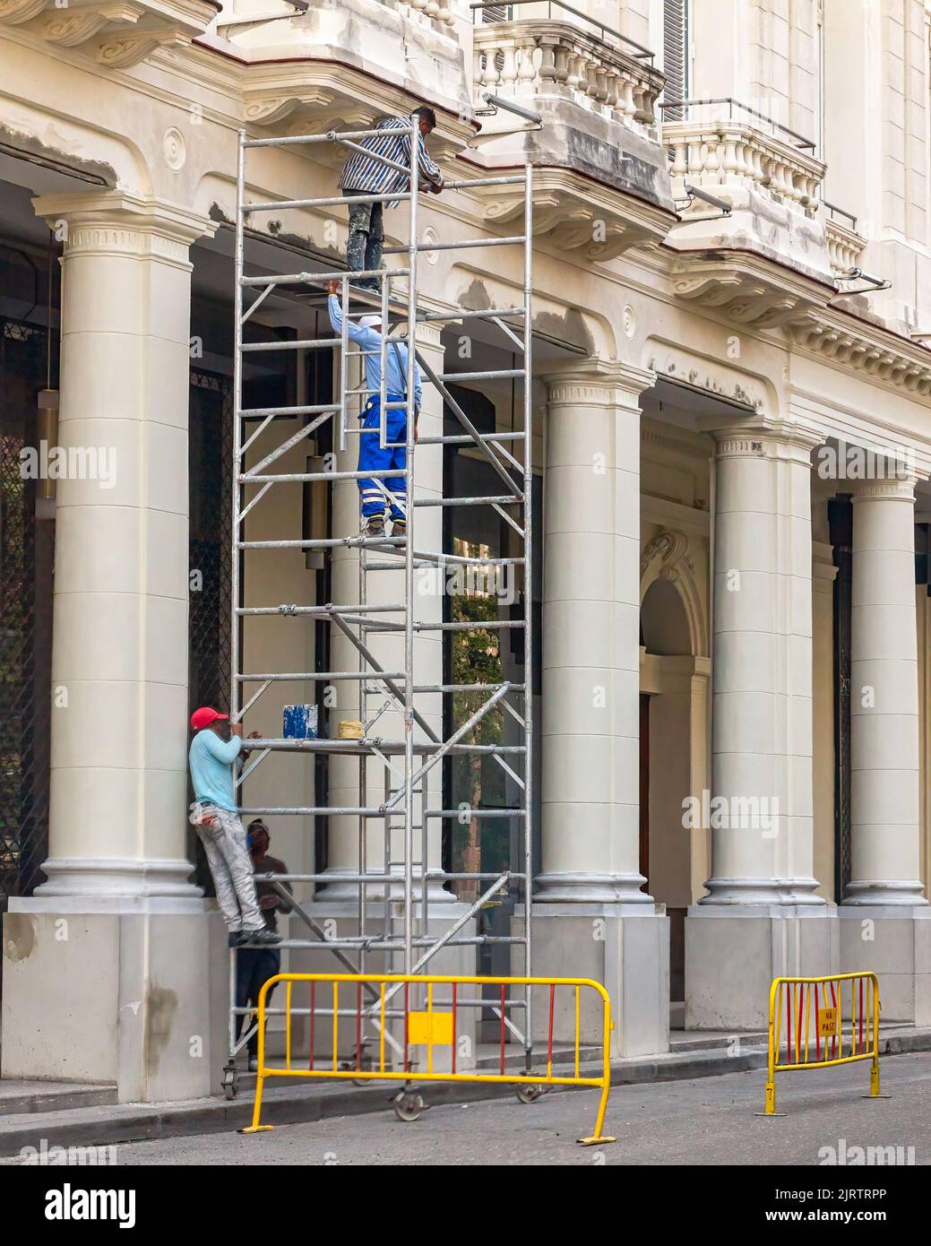 Three Cuban workers in a scaffolding are repairing or giving ...