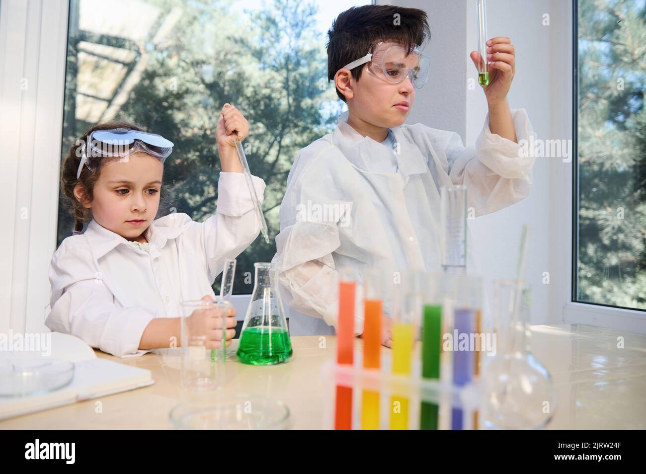 Cute boy and girl in white laboratory coats and protective eyeglasses ...